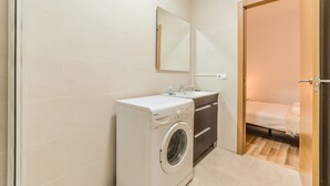 Quarto de hotel compacto com máquina de lavar, pia e cama.