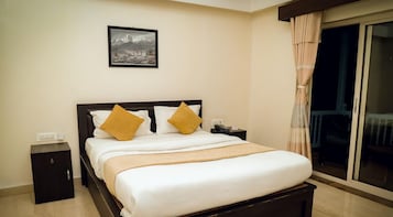 Quarto de hotel com cama, mesa de cabeceira, um quadro na parede e janela com cortinas.