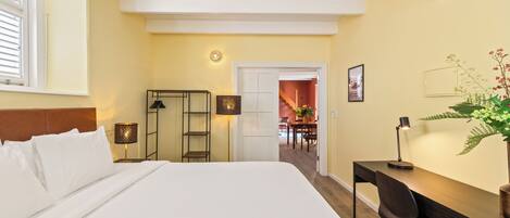 Quarto de hotel com cama, escrivaninha, cadeira, luminária e planta em vaso.