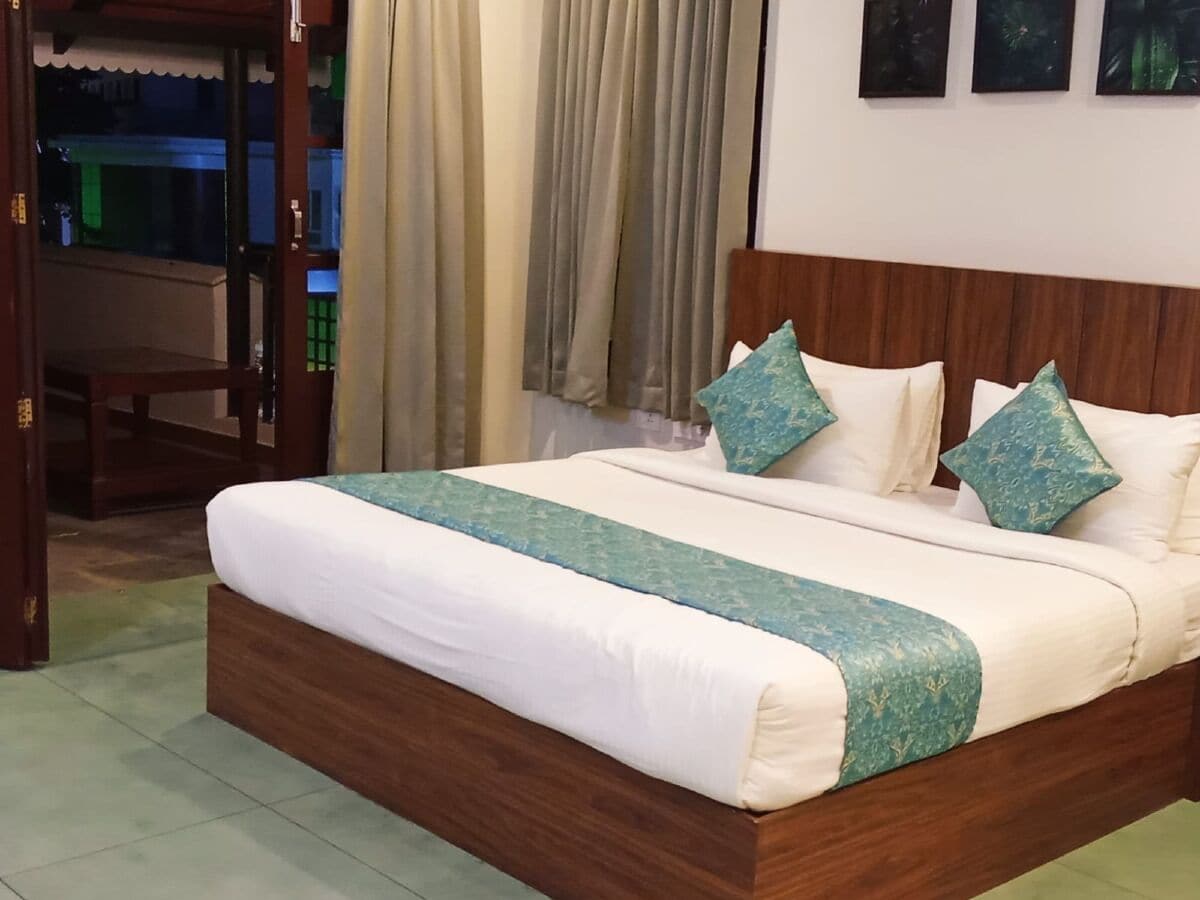 Cama bem arrumada com cabeceira de madeira, roupa de cama branca e almofadas decorativas verde-água.