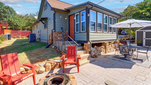 Uma casa com base de pedra, porta vermelha e um pátio com móveis de exterior.