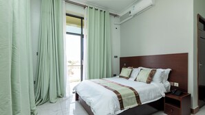 Quarto de hotel com cama, mesa de cabeceira, televisão e janela com cortinas.