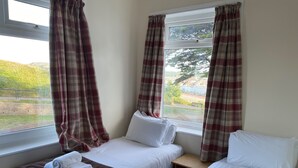 Quarto de hotel com duas camas individuais, janela com cortinas e vista para o exterior.