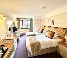 Quarto de hotel com duas camas, uma secretária com televisão e uma janela com cortinas.