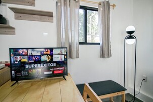 Uma sala de estar moderna com uma TV de tela plana exibindo vários títulos de filmes, um banco de madeira, um abajur e uma janela com cortinas.