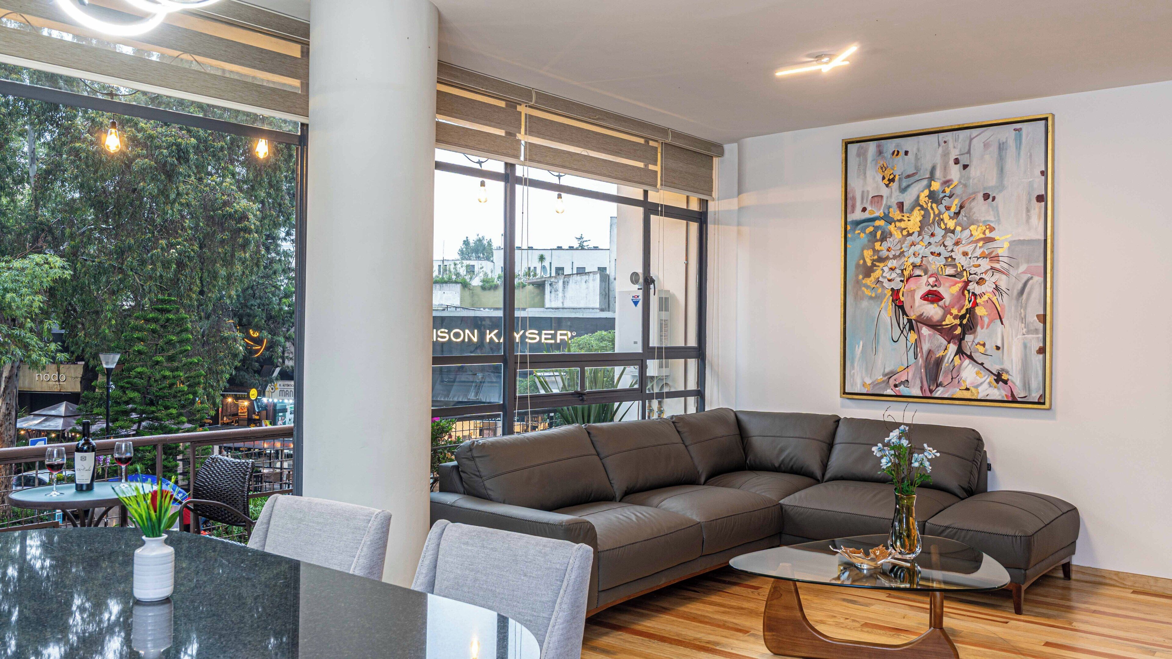 Uma sala de estar moderna com um sofá seccional, uma mesa de centro de vidro e uma grande janela com vista para o horizonte da cidade.