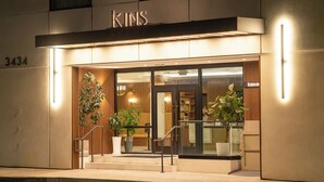 Entrada de um hotel com uma placa indicando 'KINS HOTEL', o número '3434' na parede e plantas em vasos na entrada.
