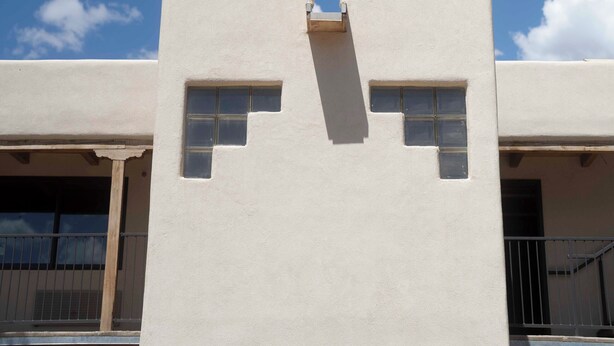 Um edifício com fachada plana, duas janelas pequenas e uma varanda com grade de metal.