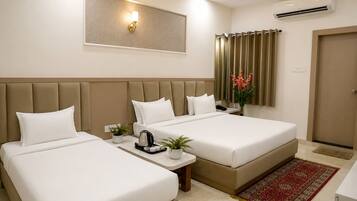 Quarto de hotel com duas camas, uma mesinha com chaleira, uma planta em vaso e um tapete vermelho.