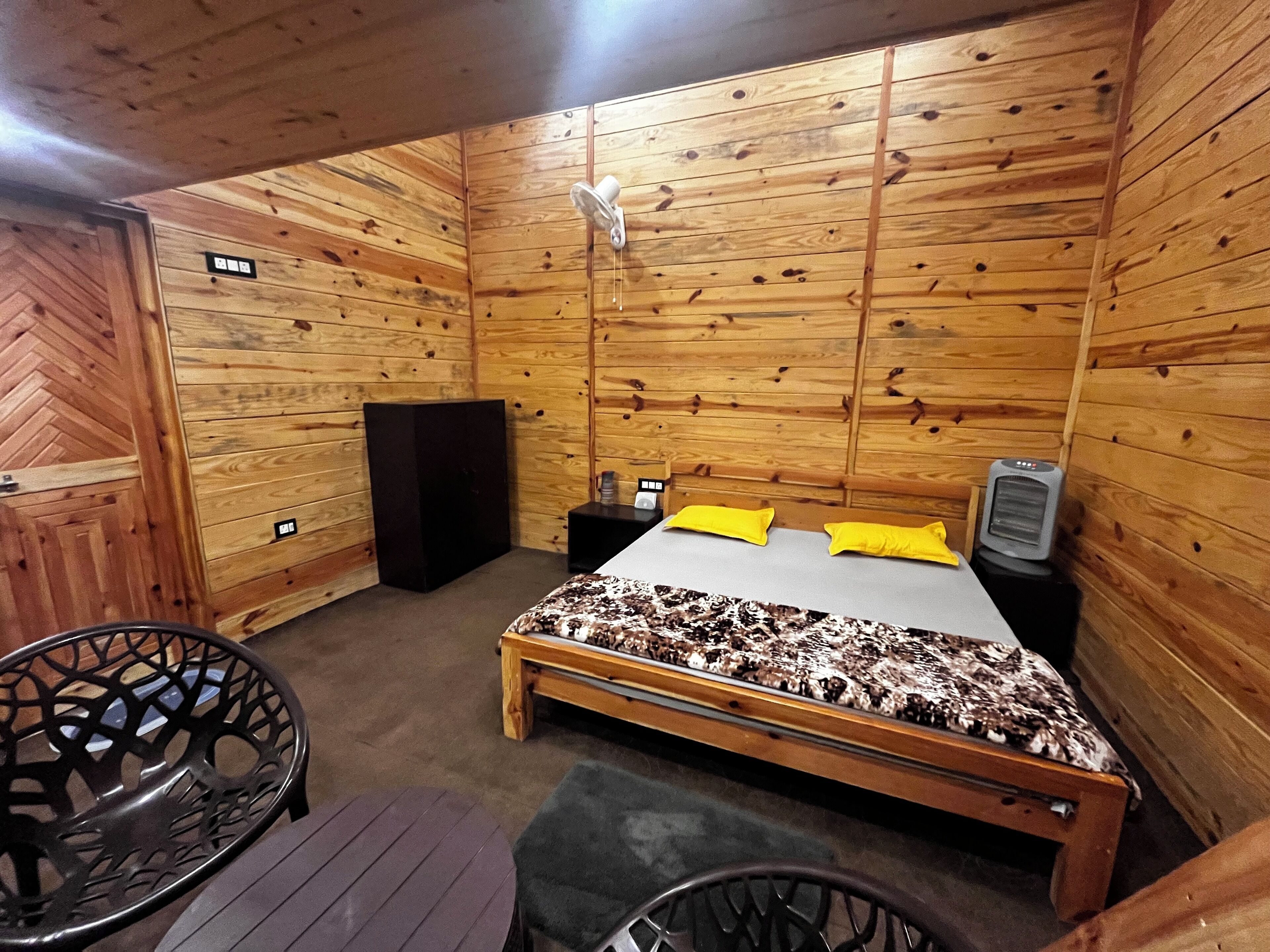Quarto com painéis de madeira, uma cama, um aquecedor, um alto-falante e uma cadeira.