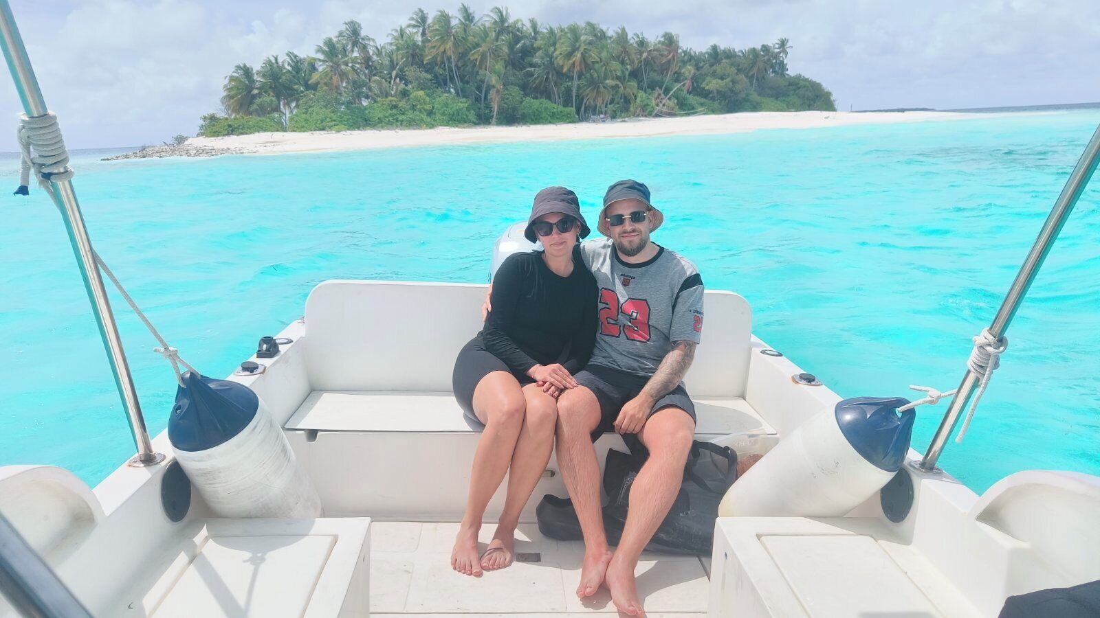 Duas pessoas em um barco, com vista para uma praia e palmeiras ao fundo.