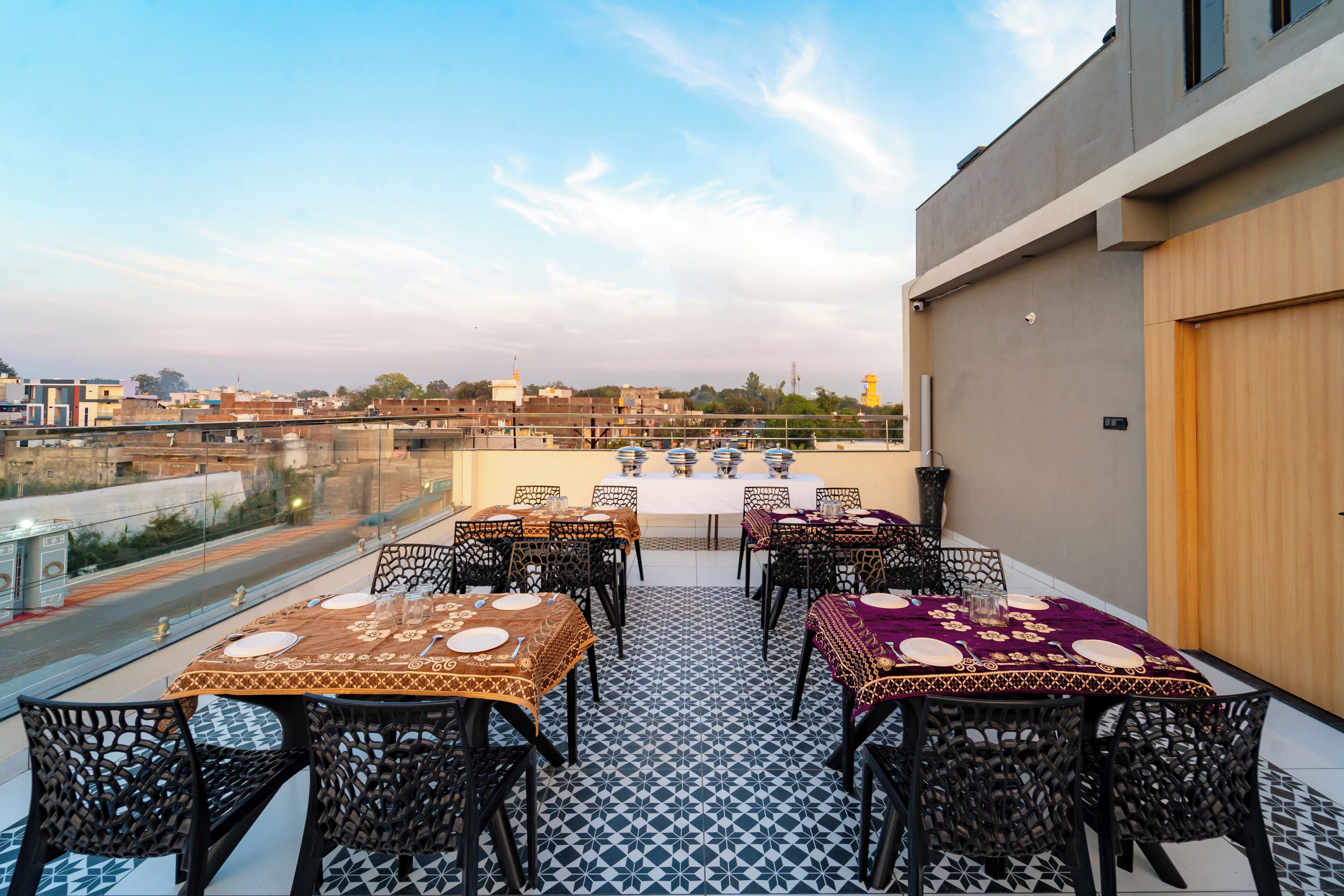 Uma área de refeições no terraço com mesas e cadeiras, piso estampado e vista para a cidade.