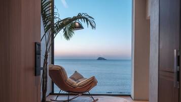 Quarto com poltrona de balanço voltada para uma grande janela com vista para o mar.