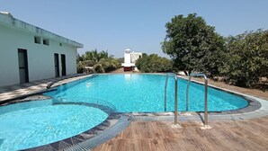 Uma piscina com um deck de madeira, cercada por vegetação e um edifício branco ao fundo.