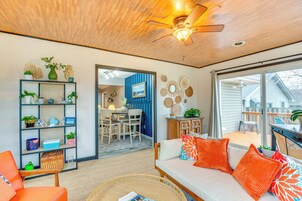 Uma sala de estar ampla com teto de madeira, ventilador de teto, sofá com almofadas laranja, estante de livros e vista para o exterior.