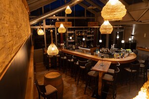 Uma área de bar com móveis de madeira, luminárias pendentes e balcão com garrafas.