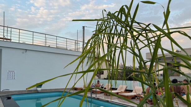 Piscina com vista para o céu e um prédio branco ao fundo.