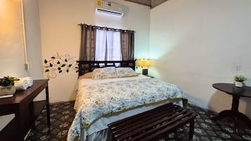 Quarto com cama, mesa de cabeceira, abajur, uma pequena mesa com uma planta e aparelho de ar condicionado.