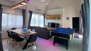 Um espaço moderno de estar com área de refeições, mesa de bilhar e cozinha compacta.
