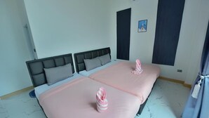 Quarto de hotel com duas camas, cada uma com um edredom rosa e uma toalha enrolada. Há duas cabeceiras pretas e um travesseiro cinza em cada cama. O quarto tem um chão com padrão de mármore e uma janela grande com uma persiana escura.