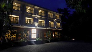 Um hotel com várias andares, varandas, uma entrada bem iluminada e uma placa.