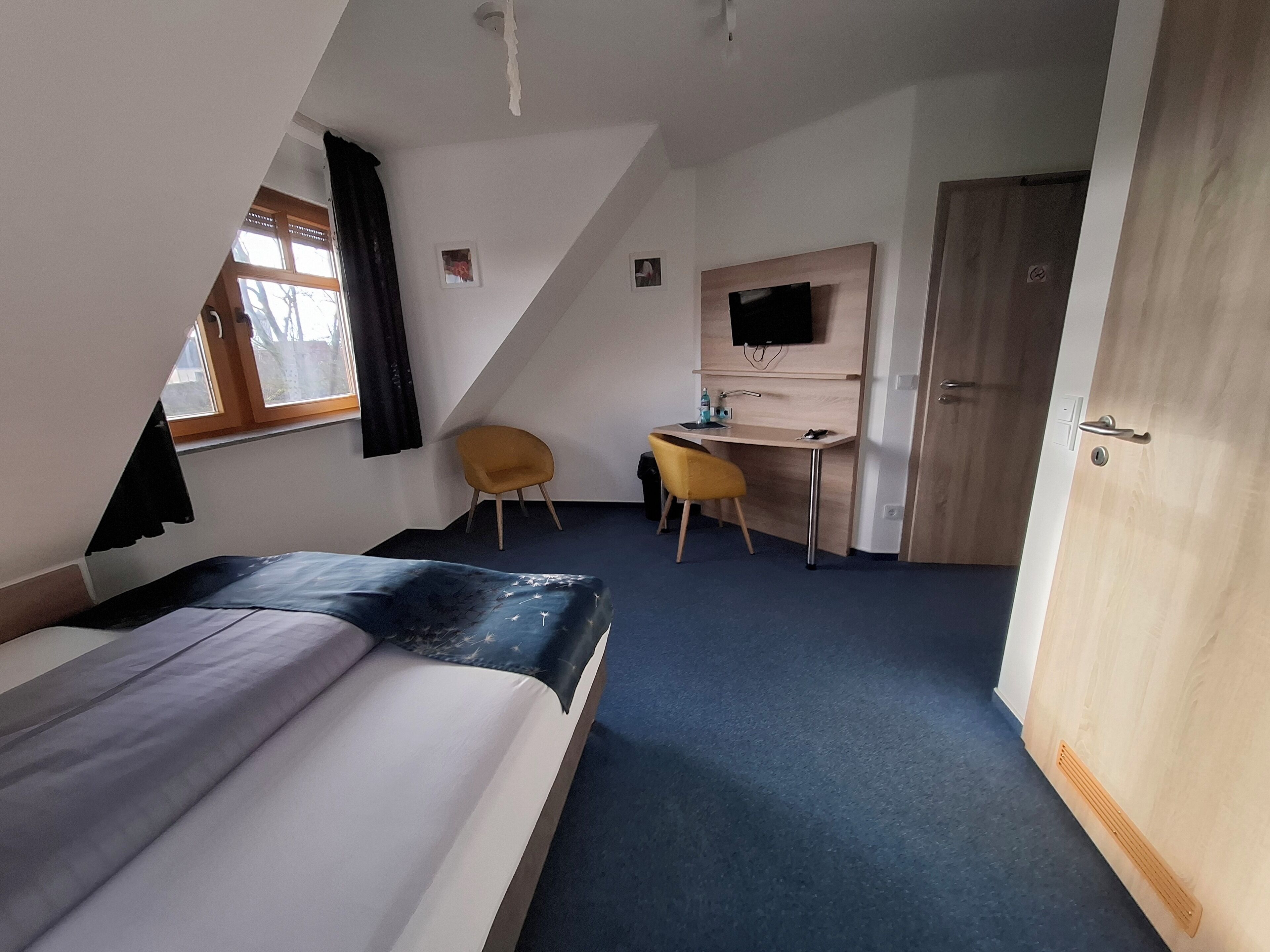 Quarto com cama, escrivaninha, cadeira, televisão e porta.