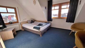 Quarto com cama, escrivaninha, cadeira, radiador e janela com cortinas.