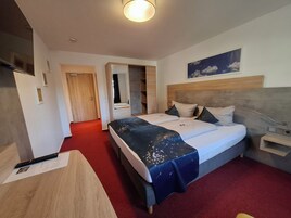 Quarto de hotel com uma cama grande, uma escrivaninha, uma cadeira, uma mesa de cabeceira e um espelho.