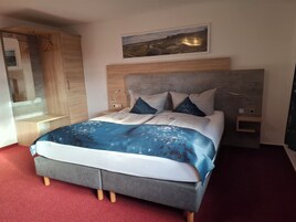 Uma cama bem arrumada com colcha azul florida, cabeceira de madeira e mesa de cabeceira com abajur.