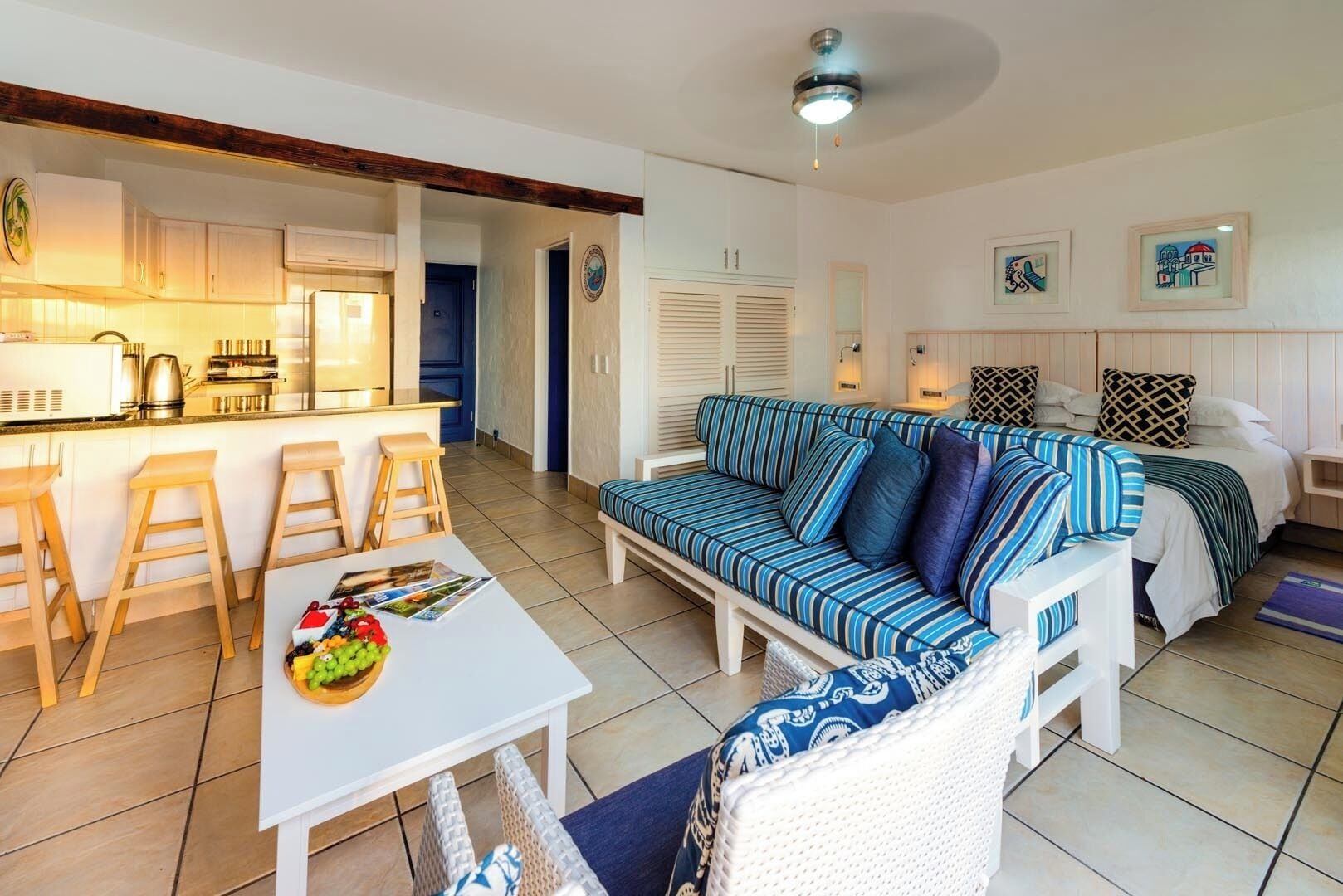 Um espaço compacto com cozinha americana, sofá listrado, área de refeições com banquetas e cama com almofadas estampadas.