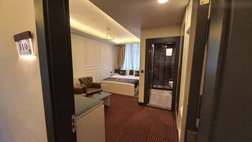 Quarto de hotel com cama, pequena escrivaninha, cadeira e chuveiro.