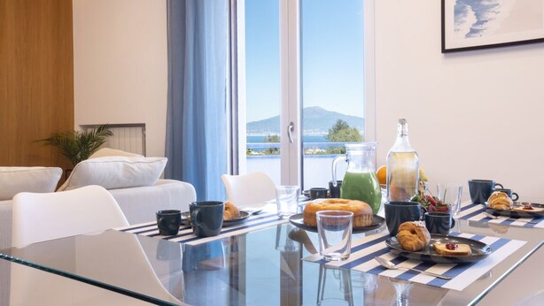 Quarto de hotel moderno com varanda, mesa de jantar posta com itens de café da manhã e vista para montanha e mar.