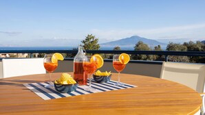 Uma mesa de madeira com bebidas e petiscos numa varanda com vista para uma paisagem montanhosa.