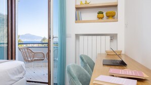 Quarto com varanda, uma cama, escrivaninha com laptop e livros.