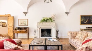 Uma sala de estar com lareira, uma escrivaninha de madeira, um sofá estampado e uma mesa de centro.
