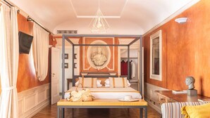 Quarto com cama de dossel, piso de madeira, luminária no teto e busto na parede.