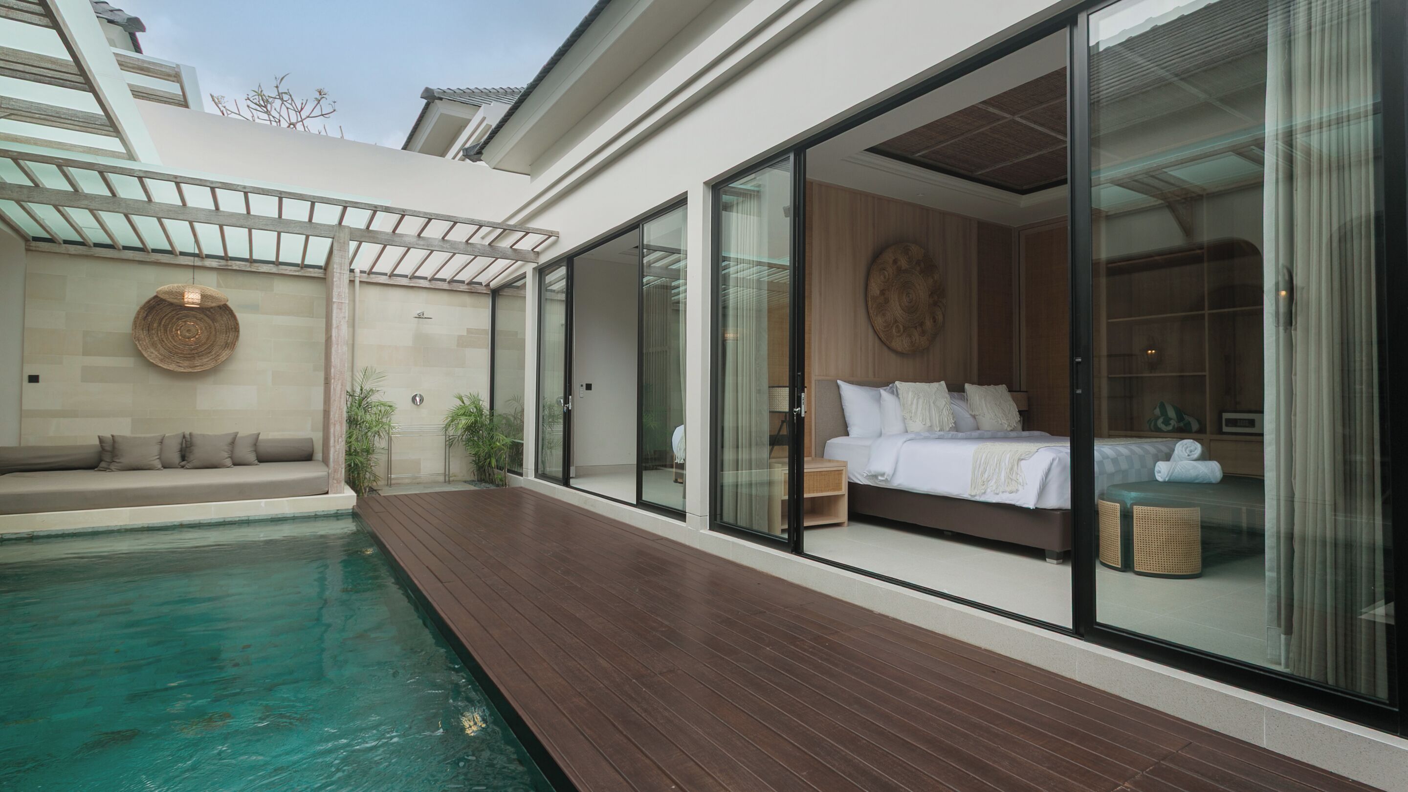 Quarto de hotel moderno com uma grande parede de vidro, deck de madeira, banheiro privativo e piscina.