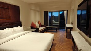 Quarto de hotel com uma cama grande, um sofá, uma mesa pequena e uma varanda com vista.