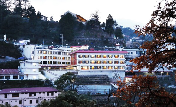 Um hotel com vários andares, teto vermelho, diversas varandas e vista para uma paisagem montanhosa.