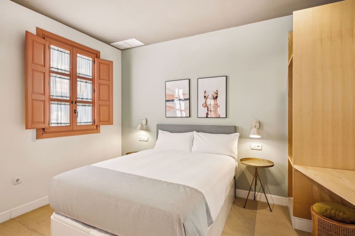 Quarto com cama, guarda-roupa de madeira, duas luminárias na parede e duas fotos emolduradas.