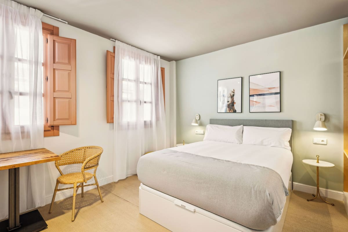 Quarto com cama, escrivaninha, cadeira e duas luminárias de parede.