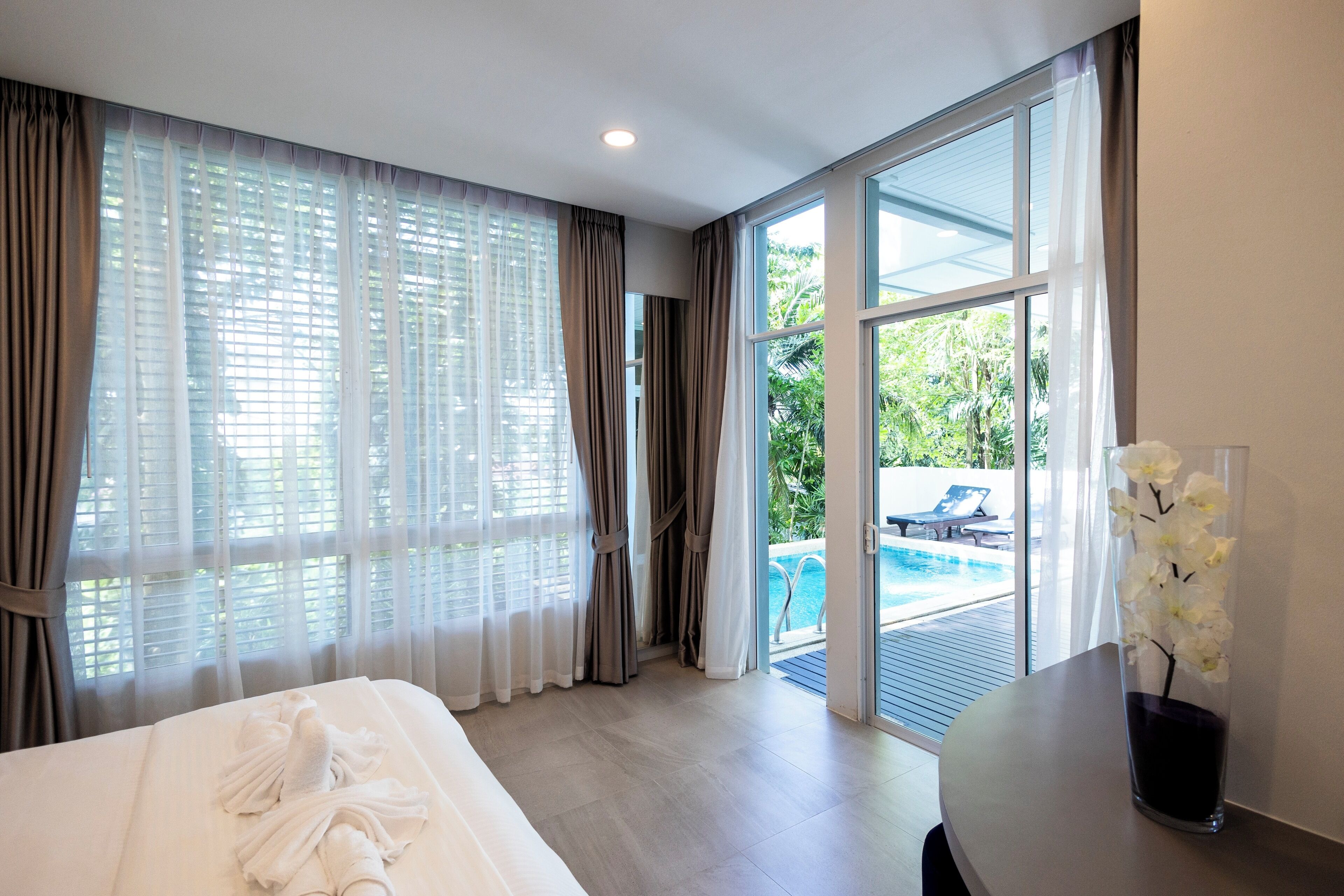 Quarto de hotel com cama, um vaso de flores e vista para uma piscina.