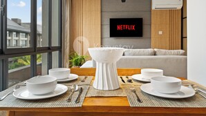 Uma sala de jantar moderna com uma mesa posta para quatro pessoas, um ventilador de teto e uma TV na parede exibindo 