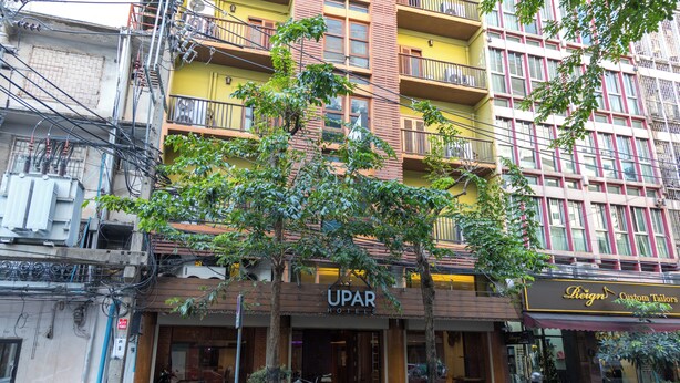 Um hotel chamado "UPAR" com entrada visível, uma motocicleta estacionada na frente e um prédio vizinho com a placa "Reign Custom Tailors".