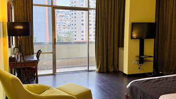 Quarto de hotel com uma cama, poltrona amarela, escrivaninha com luminária e televisão.