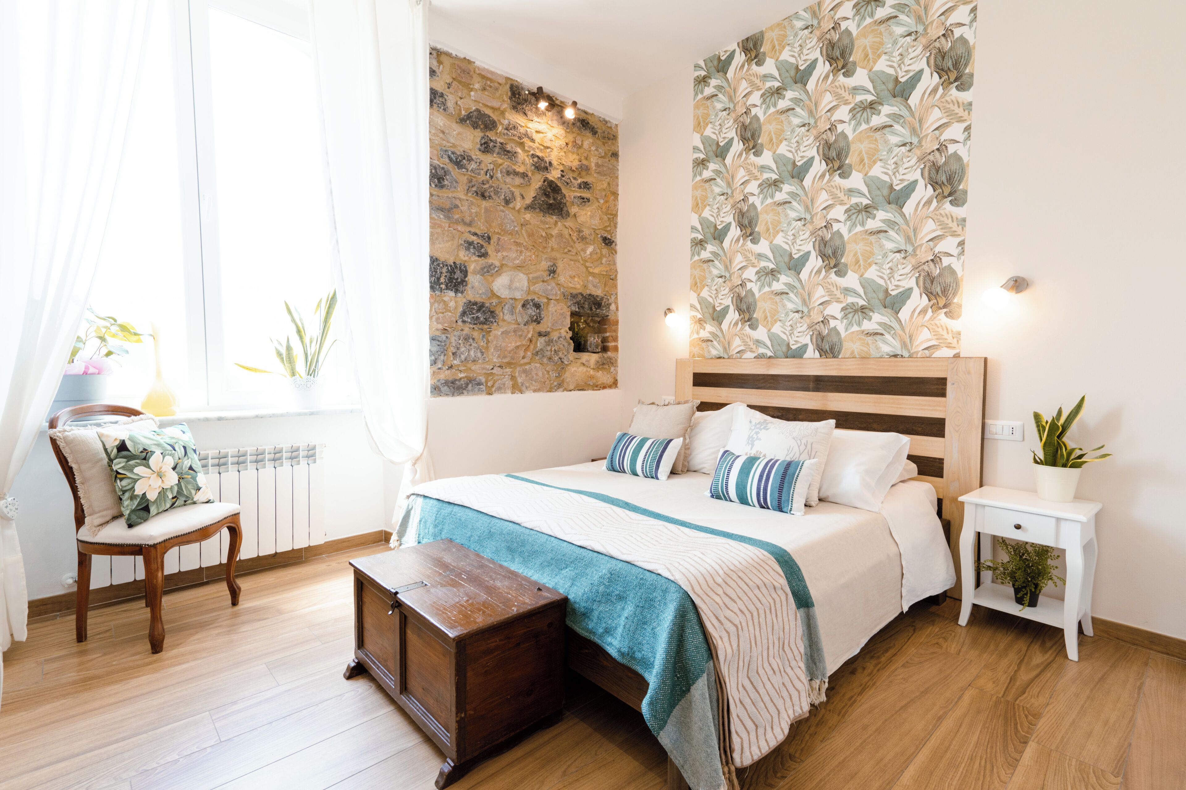 Quarto com parede de pedra, cama com roupa de cama listrada, mesa de cabeceira de madeira e janela com cortinas.