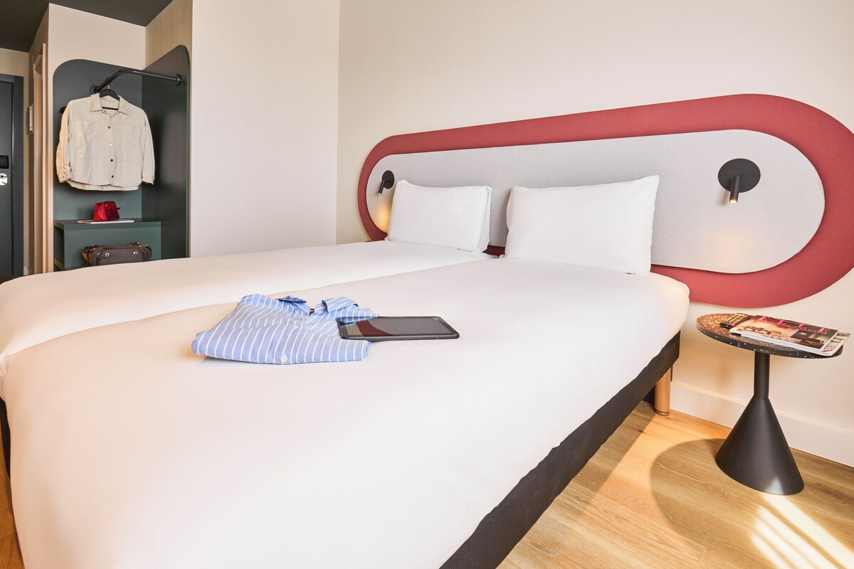 Cama bem arrumada com roupa de cama branca, um smartphone e uma camisa listrada sobre a cama.