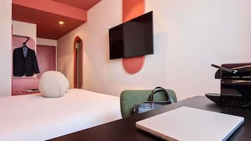 Quarto de hotel com cama, escrivaninha com laptop, televisão na parede e cabideiro com terno.