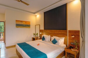 Quarto de hotel com uma cama grande, cabeceira de madeira, mesa de cabeceira com um telefone e um vaso, e um quadro na parede.