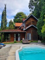 Uma casa de madeira com piscina, alpendre coberto e varanda.